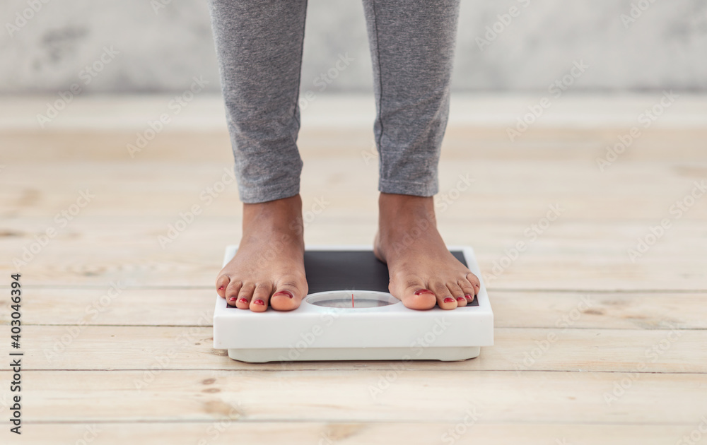 Closeup of young African American woman standing on scales indoors ...