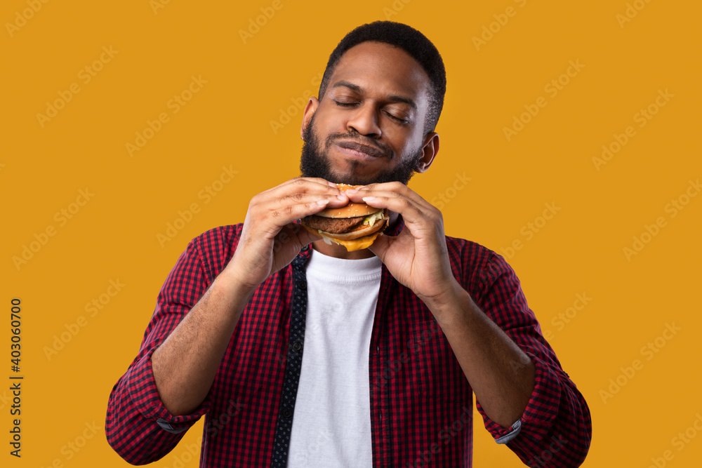 Happy African Man Eating Burger Posing Over Yellow Studio Background ...