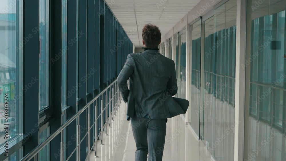 Young businessman running along long office corridor with window ...