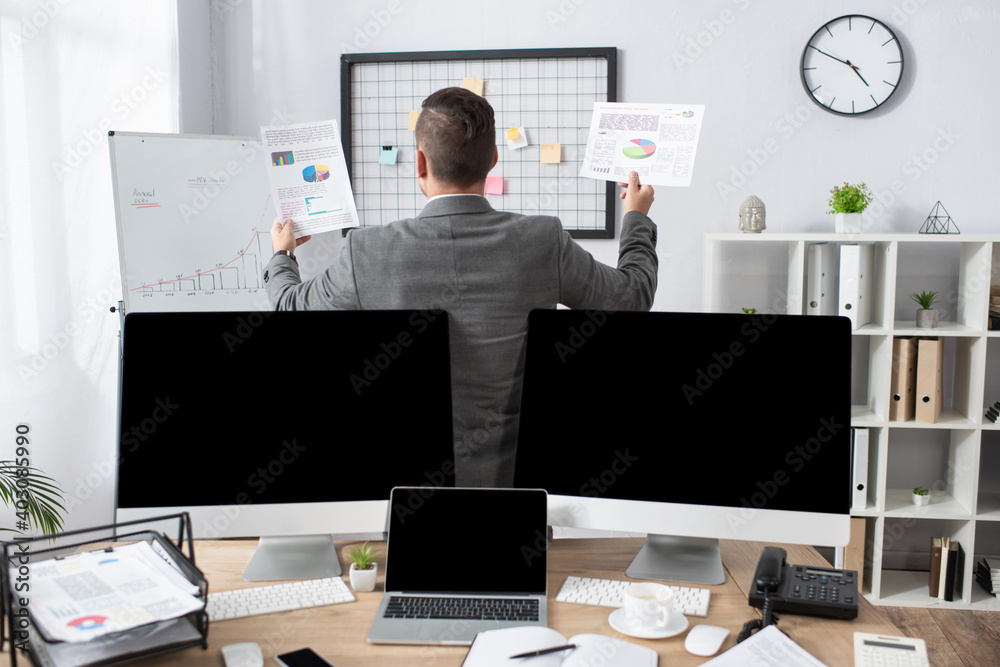 back view of trader holding infographics near monitors with blank ...