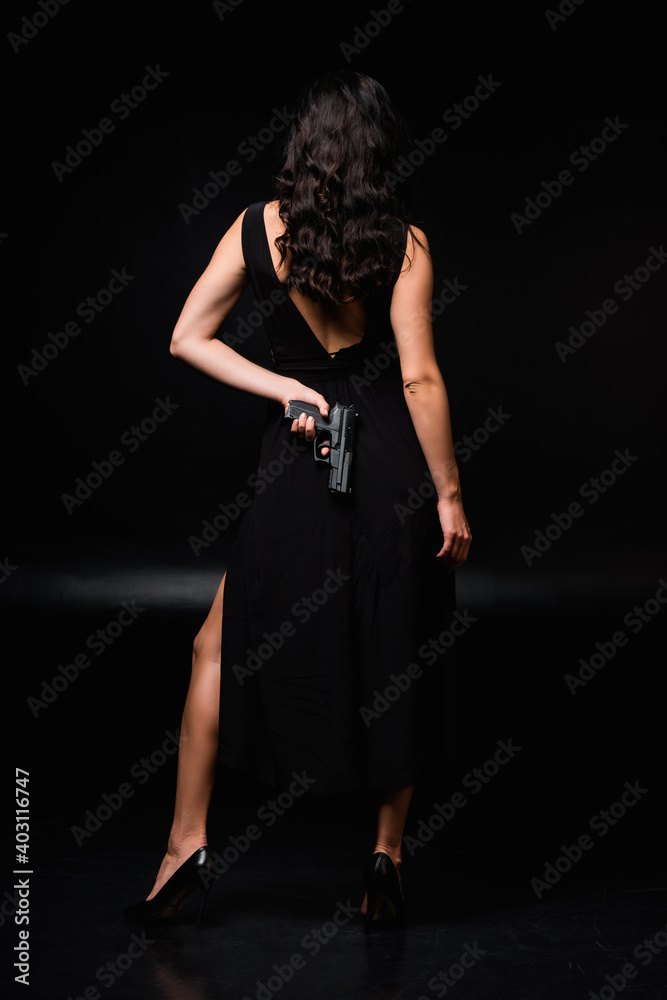 back view of dangerous woman holding gun behind back on black Stock ...