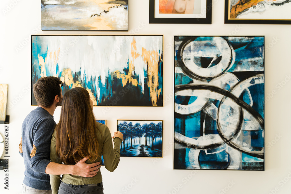 Rear view of a young woman and guy admiring the paintings of an art ...