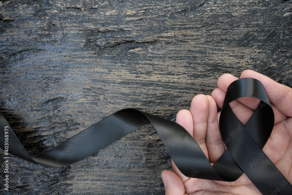 Top view of male hand holding black ribbon on dark wood background with ...