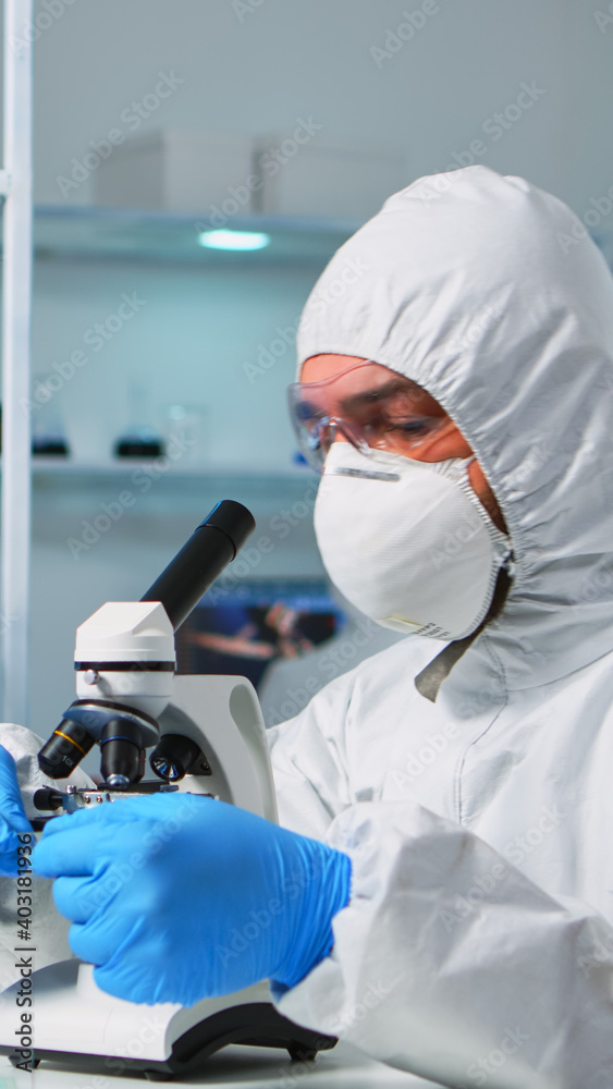 Scientist in ppe suit placing a slide on specimen stage of a laboratory ...