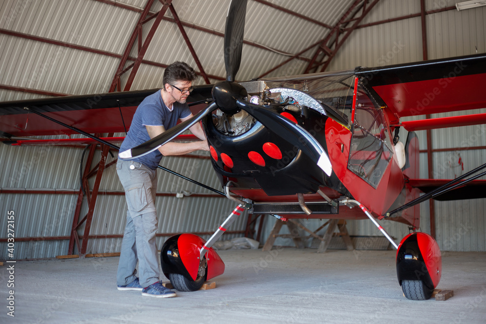 Repairman looking over engine in small aircraft from below. Small red ...