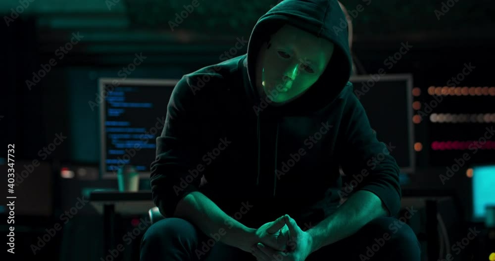 Wanted Hacker with Masked Face looks into the Camera. In the Background ...