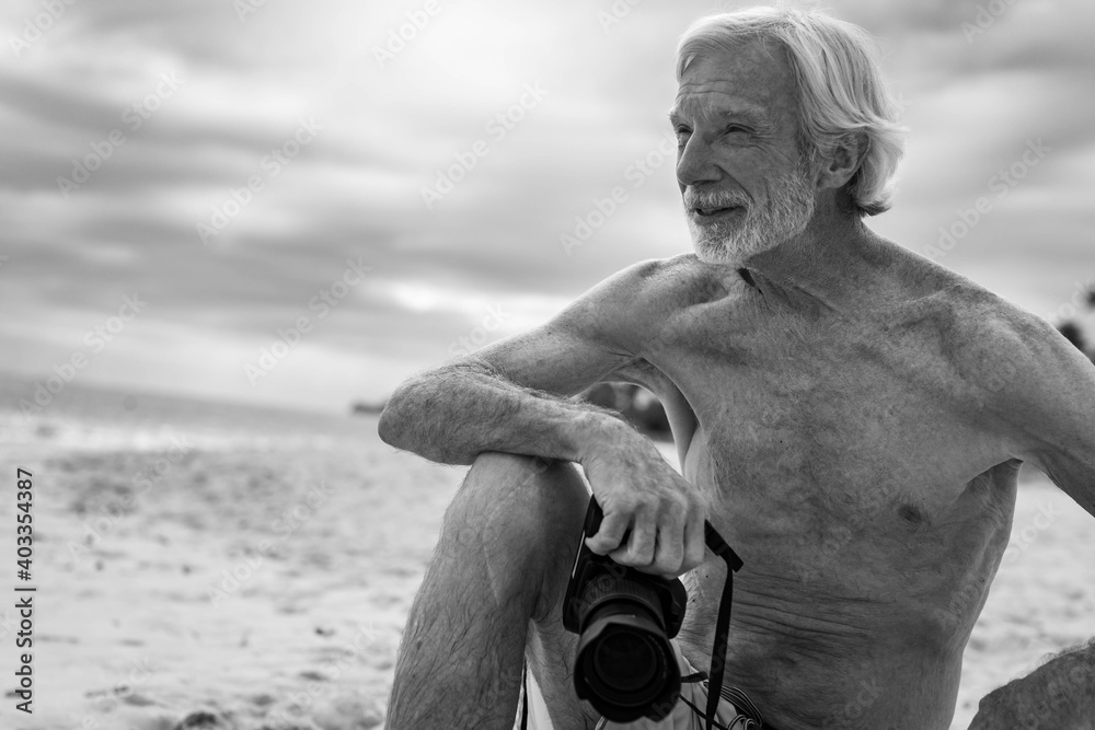 Old senior handsome active man sitting outdoor holding a camera ...