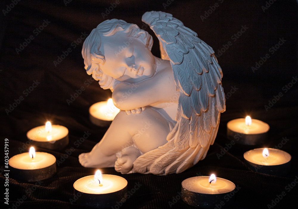 angel sculpture surrounded by burning candles; grief and loss memory of ...