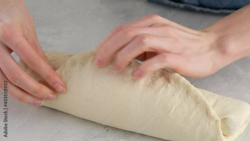 Female hands roll the dough into a roll on a light table for making ...