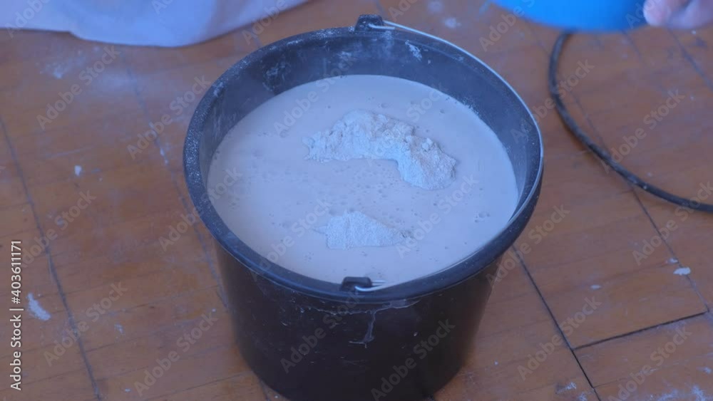 Builder is applying dry plaster and water, mixing it in bucket using an ...
