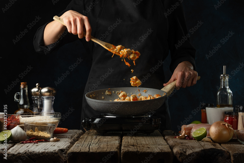 Chef in black uniform stir frying chicken fillet in the pan. Backstage ...