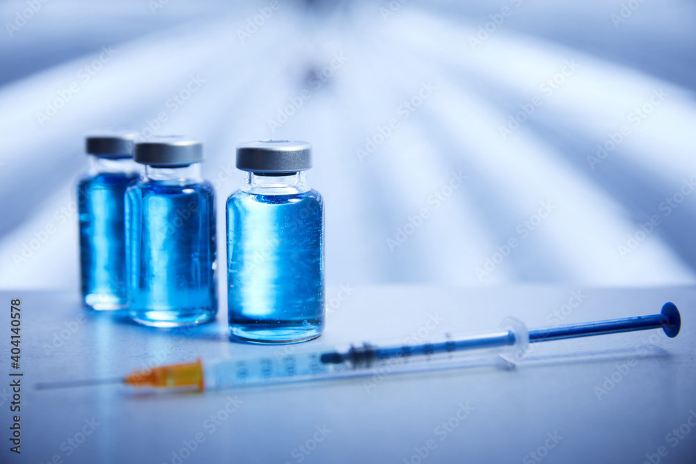 Vials of blue liquid holding vaccine lay on a metal medical surface ...