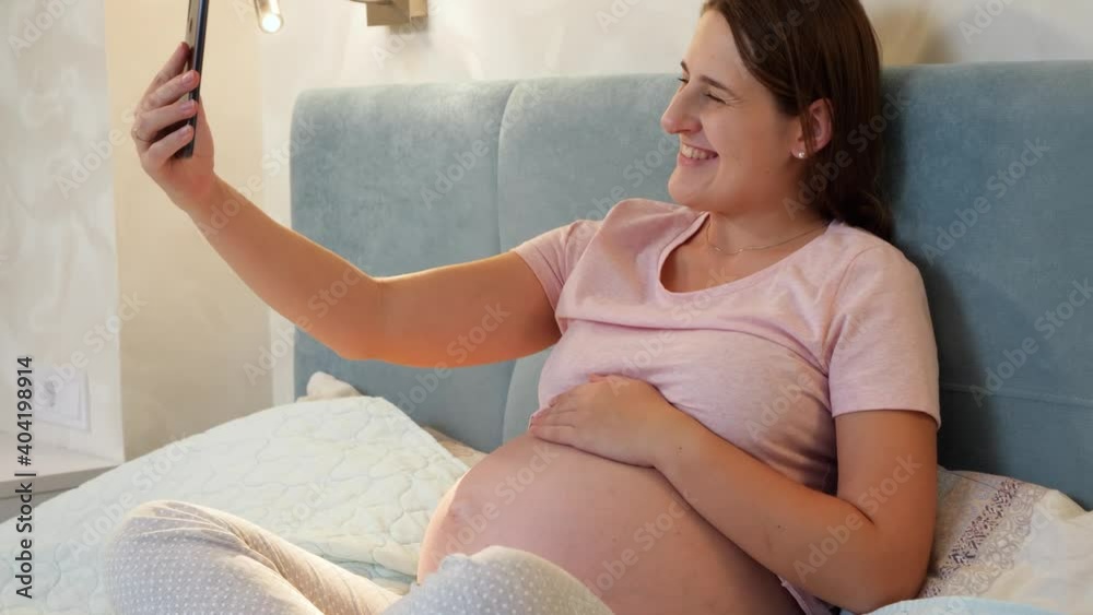 Happy Smiling Pregnant Woman Lying In Bed And Talking To A Friend On