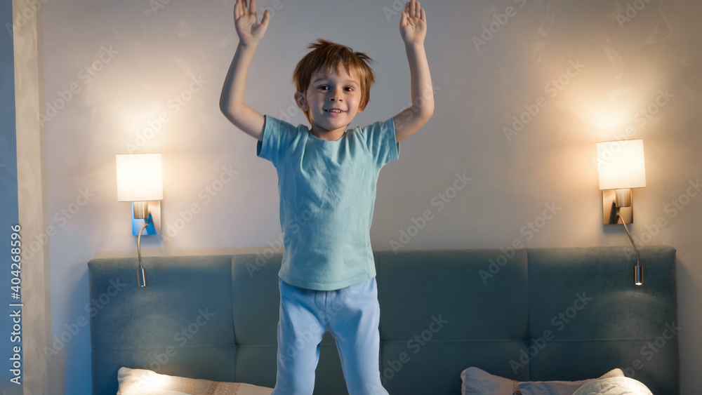 Funny little boy in pajamas jumping and dancing on parent's bed at ...
