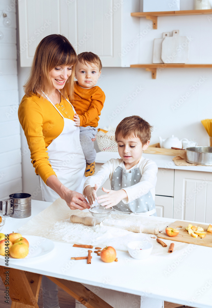 Smiling loving mother and little son wearing aprons are sowing flour ...