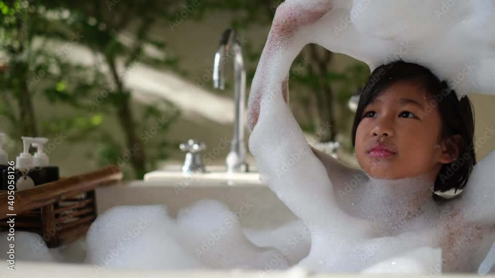 Happy asian girl take bublble bath and play with soapy foam on her head ...