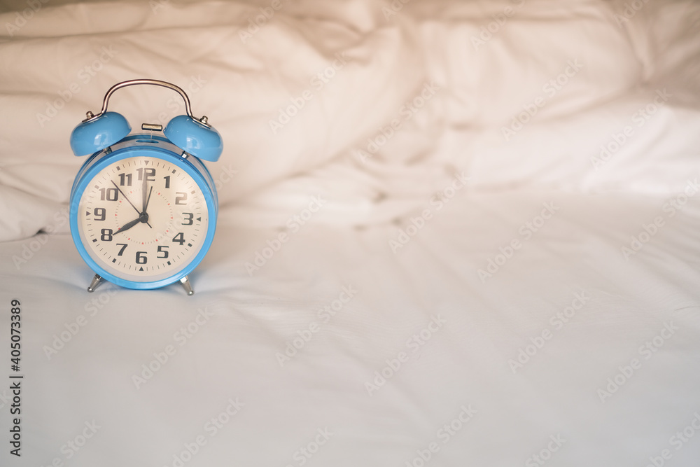 Blue vintage alarm clock on the bed at home with sunlight effect. Wake ...