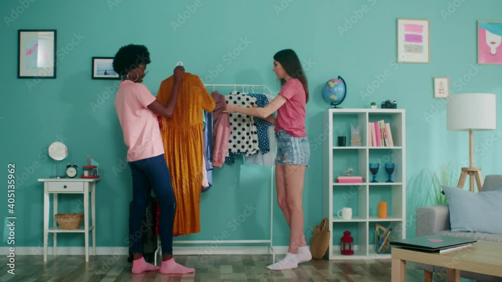 Young women, best friends, are standing near the clothes rack at home ...