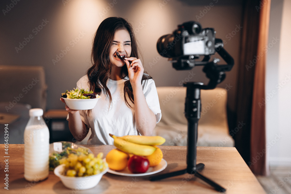 Healthy food blogger young female eating fresh vegan salad in kitchen ...