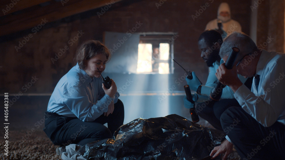 Diverse team of police officers squatting and examining dead body at ...