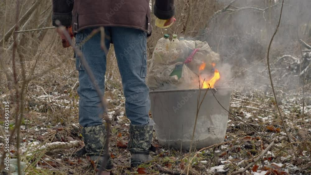 A man is pouring fuel over plastic garbage. A homeless man burns trash ...