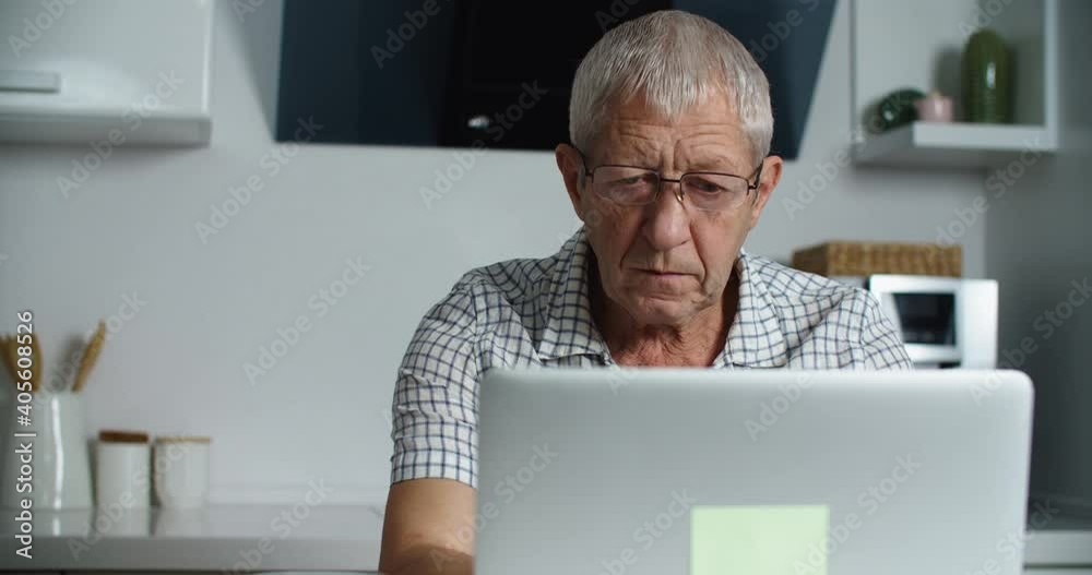 Tired Elderly man with glasses works on a laptop at home, takes off his ...