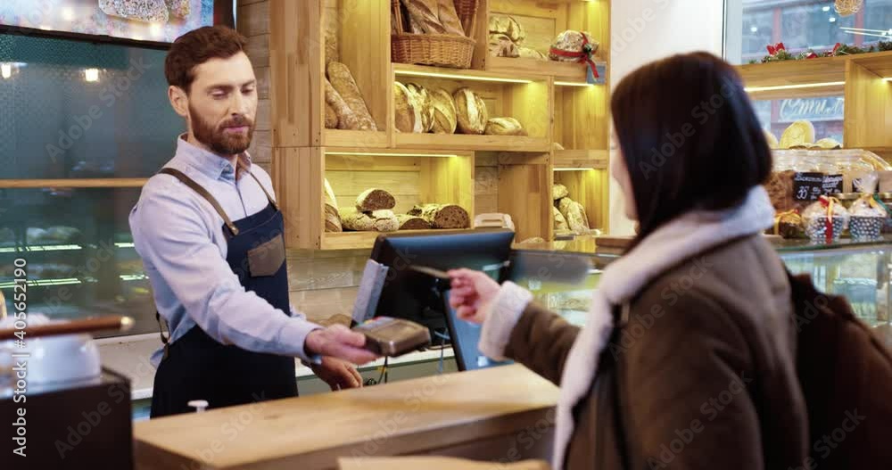 Happy baker owners work together and serves client. Woman gives goods ...