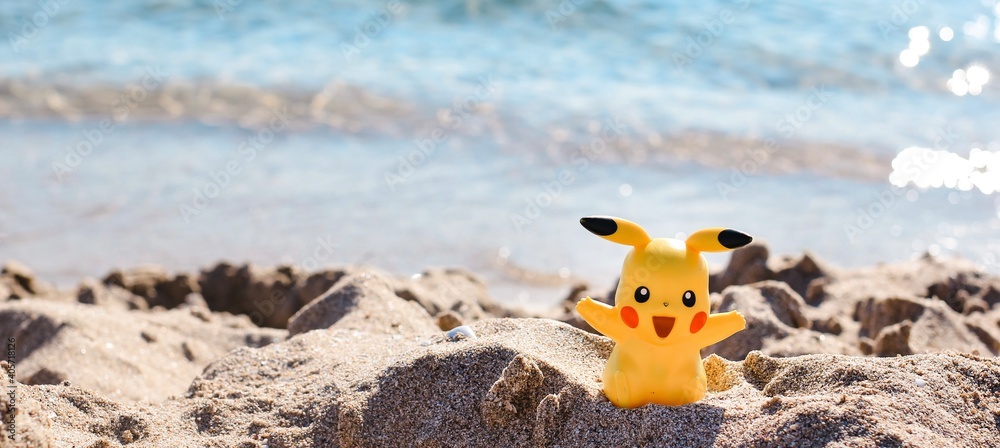 Pikachu figure model sitting on a sandy beach by the sea. Banner. Stock ...