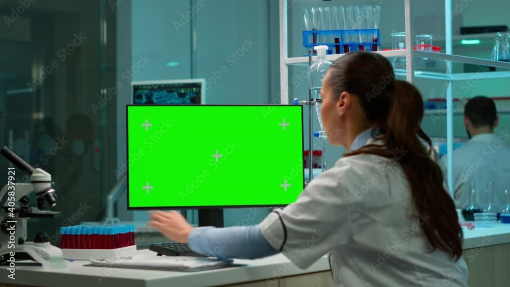 Scientist analysing blood sample and typing at computer with green ...