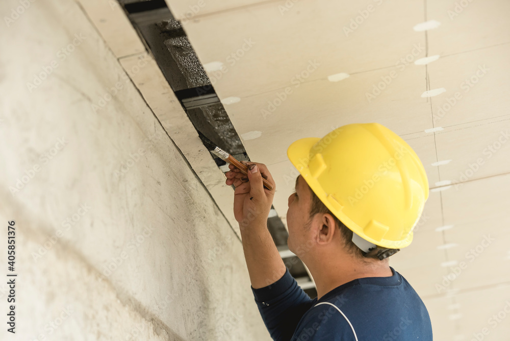 A construction worker paints some exposed metal furring holding the ...