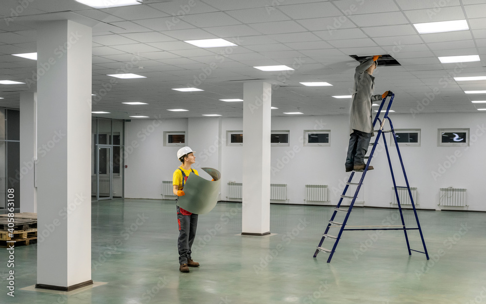 Workers on a ladder check the electrical wires on the ceiling. Workers ...