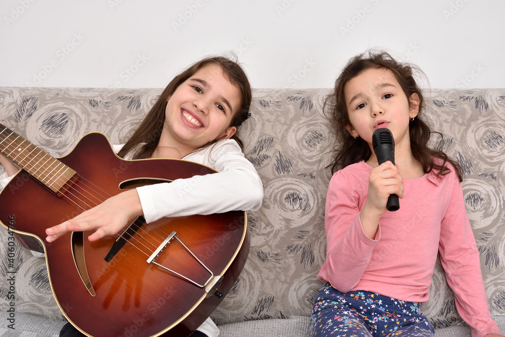 Two happy smiling sisters sitting on the sofa and singing. Older sister ...