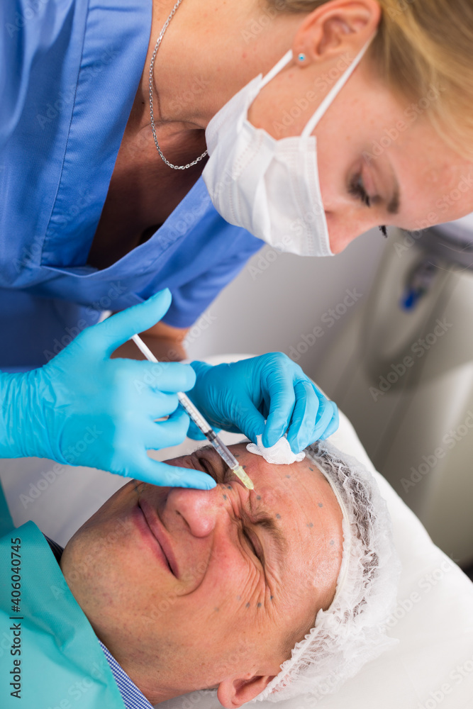 Female doctor is doing injection to patient in skin of face in estetic ...