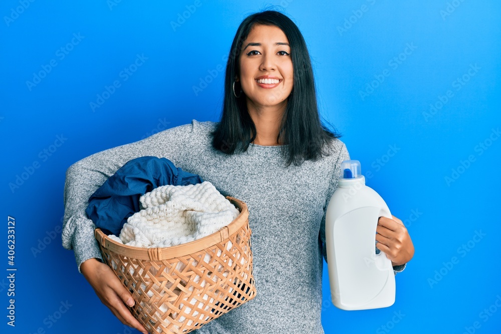 Beautiful asian young woman holding laundry basket and detergent bottle ...