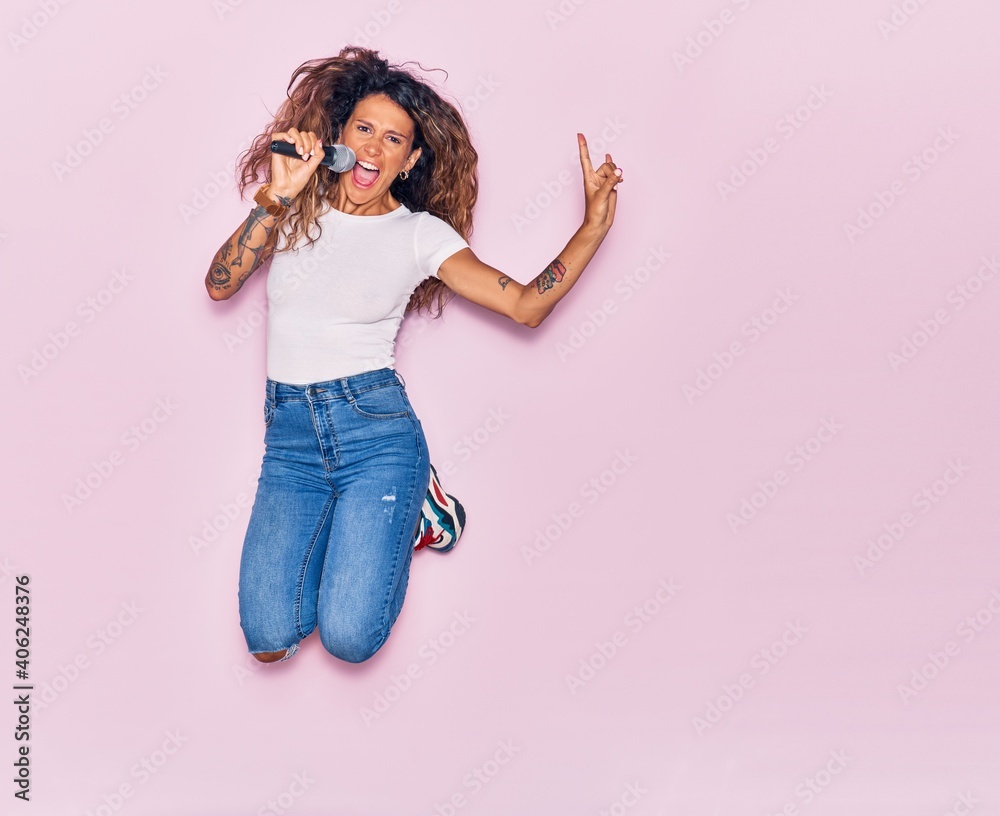 Young beautiful curly singer woman with tattoo smiling happy. Jumping ...