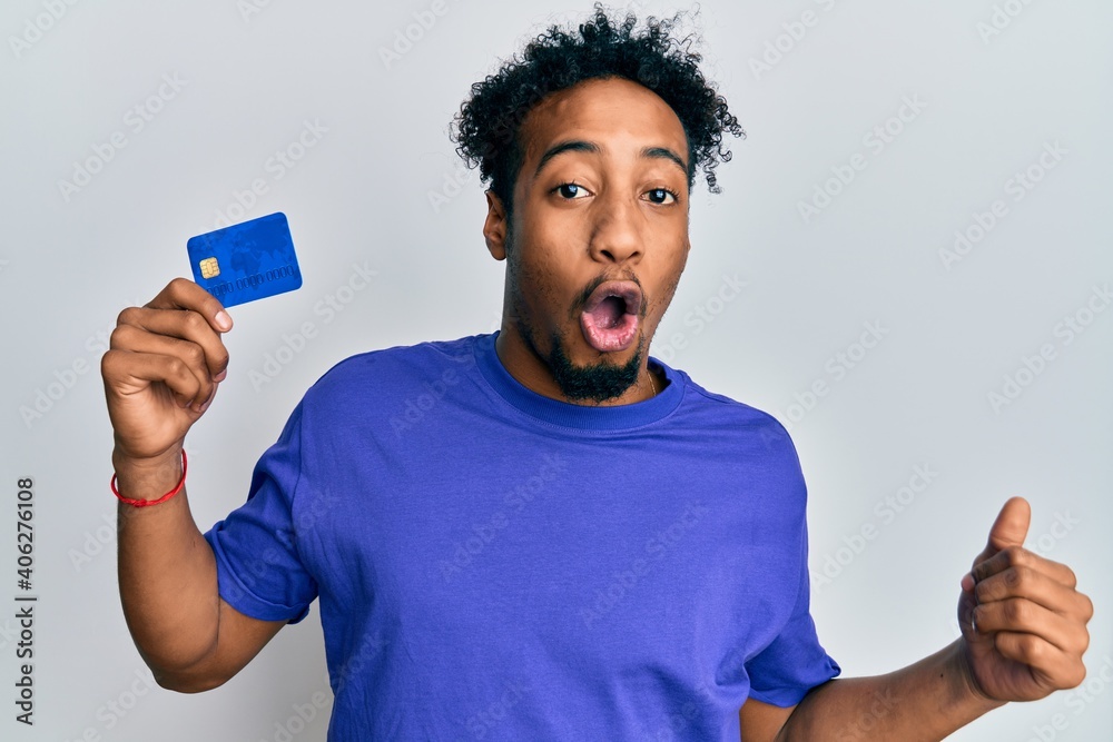 Young african american man with beard holding credit card scared and ...