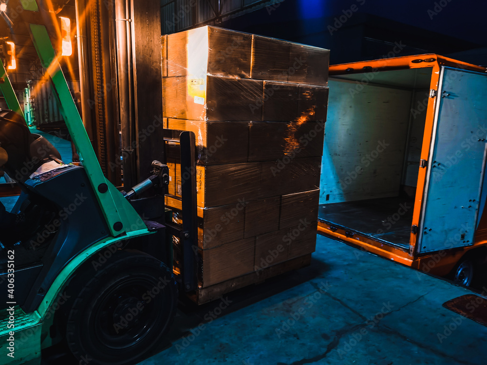 Worker driving forklift loading shipment carton boxes goods on wooden ...