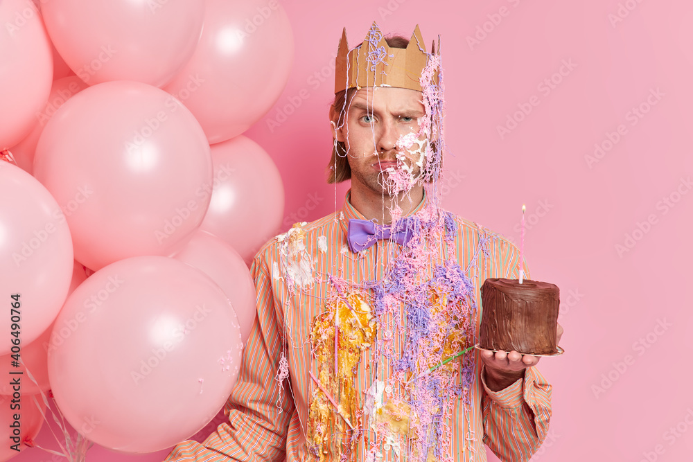 Unhappy displeased man frowns face looks angrily at camera holds cake ...