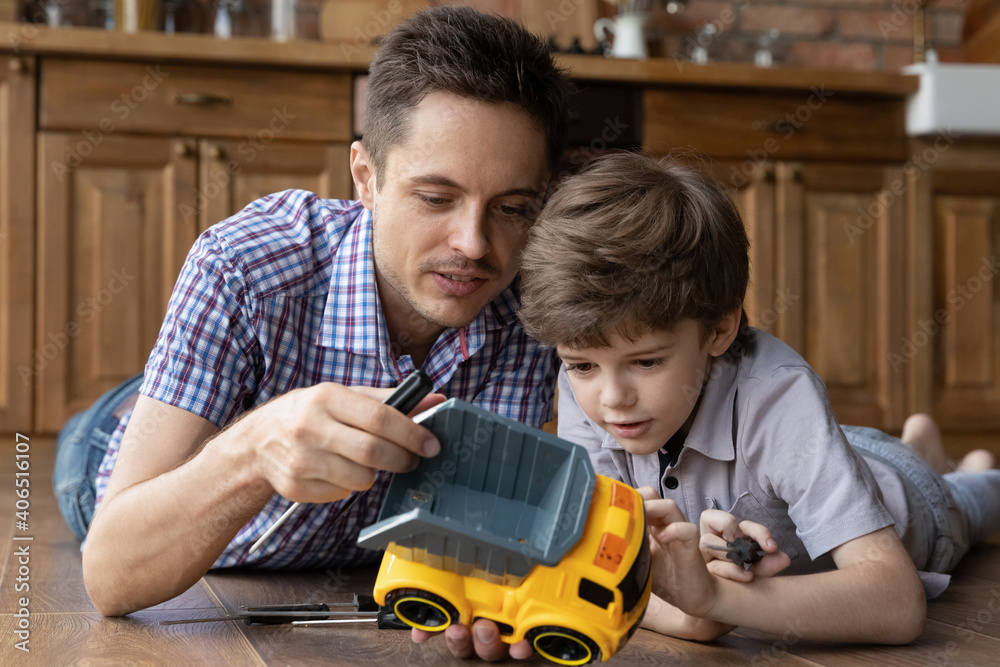Caring young Caucasian father and little 6s son have fun fixing toy car ...