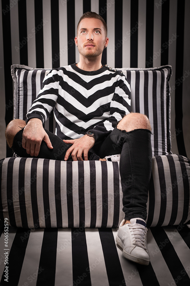 fashion guy in graphical stripes studio sit on chair and poses serious ...
