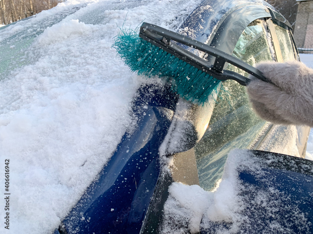 Cleaning the car from snow with a brush. In the photo, the girl cleans ...