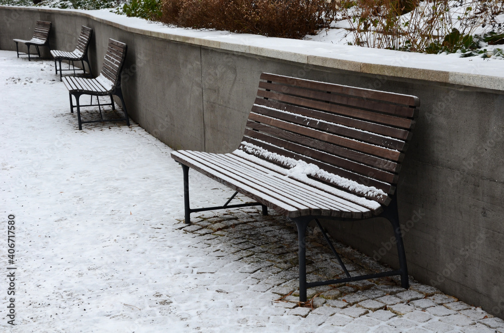 snowy benches near the supporting concrete gray wall in the park ...