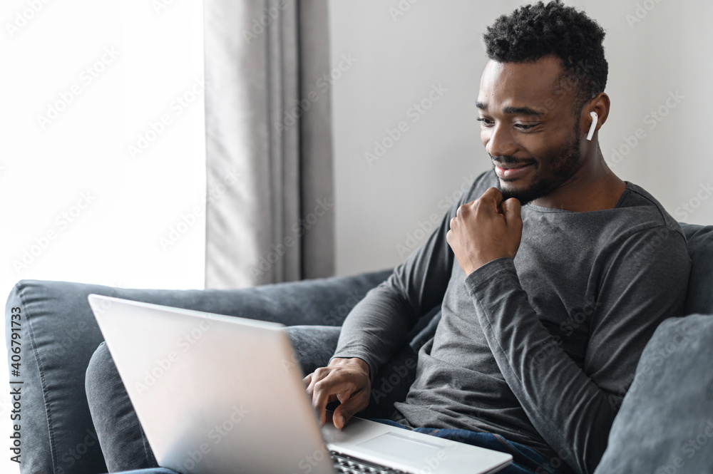 Photo Art Print A cheerful smiling African American guy sits with laptop on comfortable couch an Vadim Pastuh
