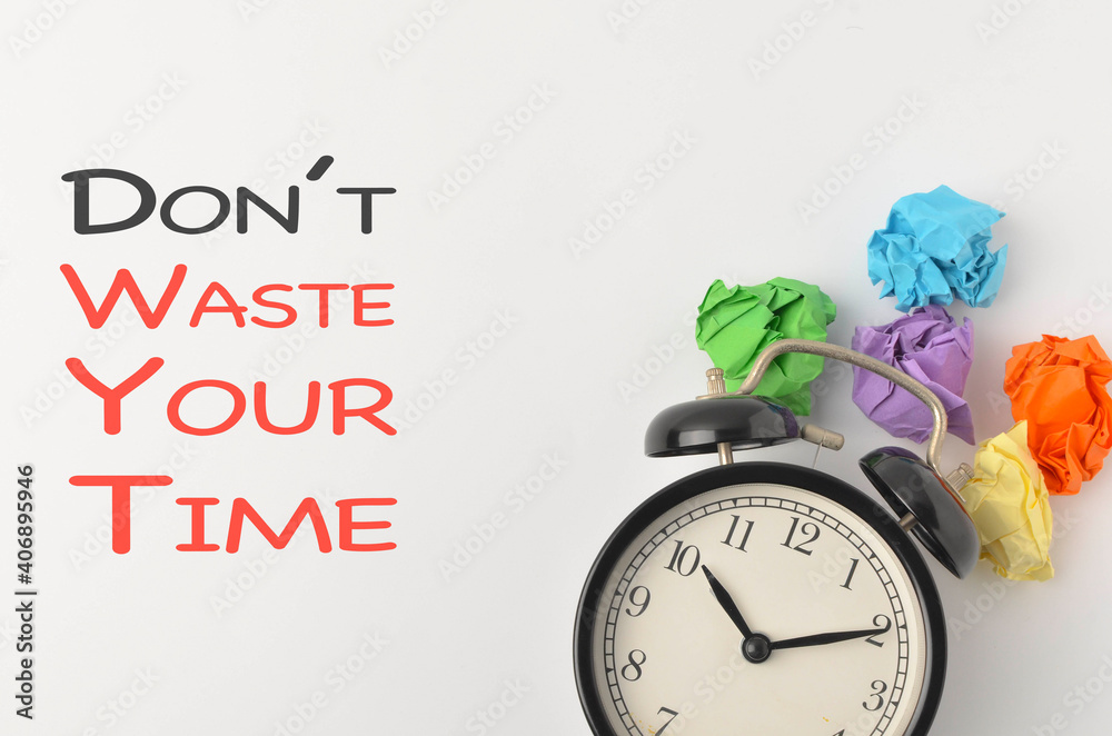 Dont Waste Your time written with alarm clock and paper trash on white ...