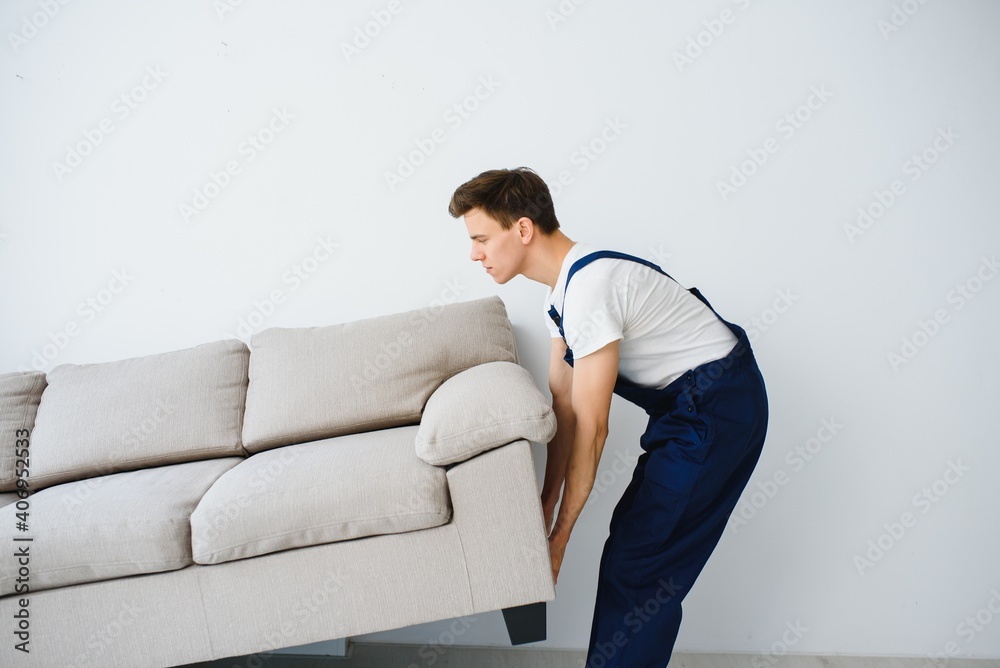 Loader moves sofa, couch. worker in overalls lifts up sofa, white ...