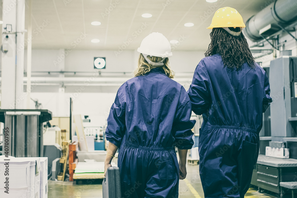 Diverse female factory workers in hardhats and overalls walking on ...