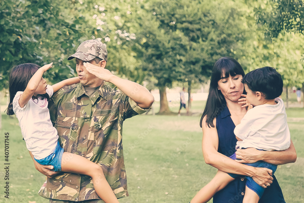 Positive military man walking in park with his wife and children ...