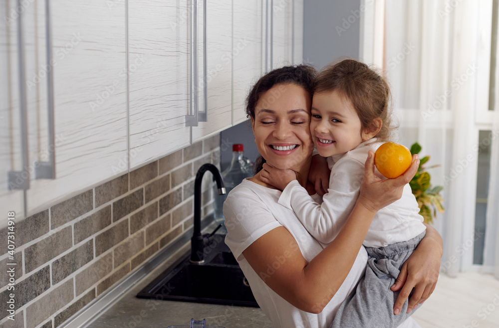Happy mother hugs her little daughter standing in the kitchen while ...