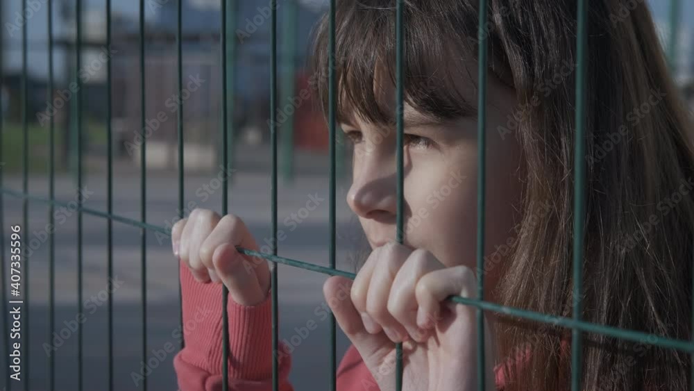 Reflective adolescence. A view of an upset child staying by the grid in ...