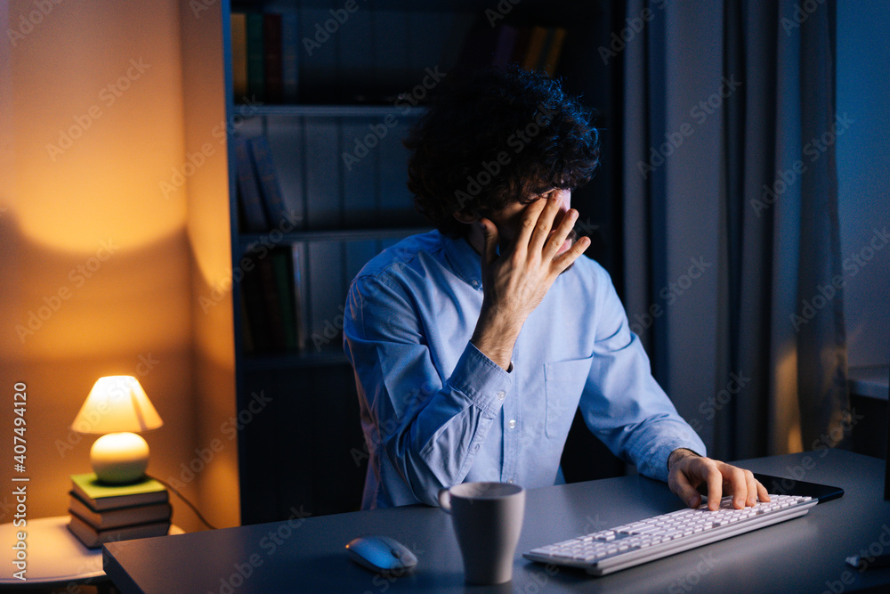 Tired young man working using computer then puts his head on keyboard ...